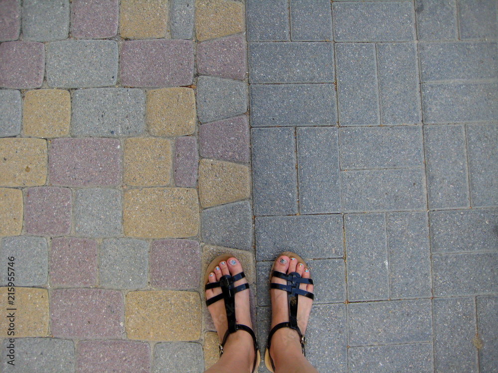 Legs in sandals on the path of two types of paving tiles of different ...