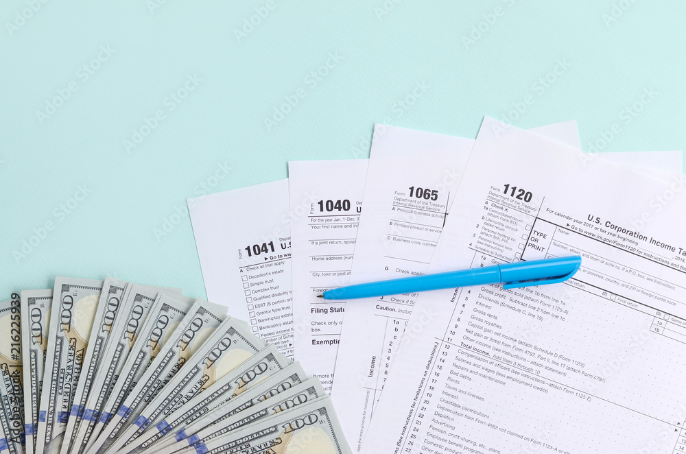 Tax forms lies near hundred dollar bills and blue pen on a light blue ...