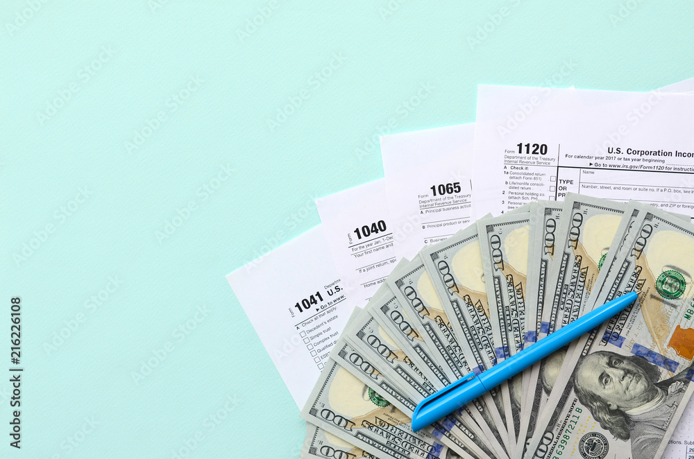 Tax forms lies near hundred dollar bills and blue pen on a light blue ...