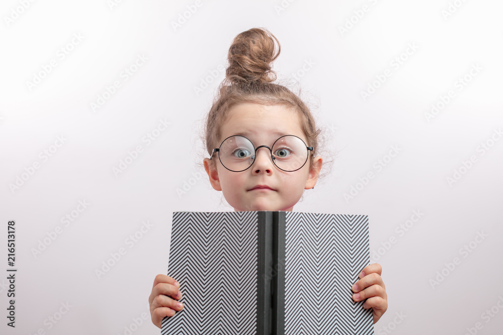 little girl with hairbun trusting out her head from the opened book ...