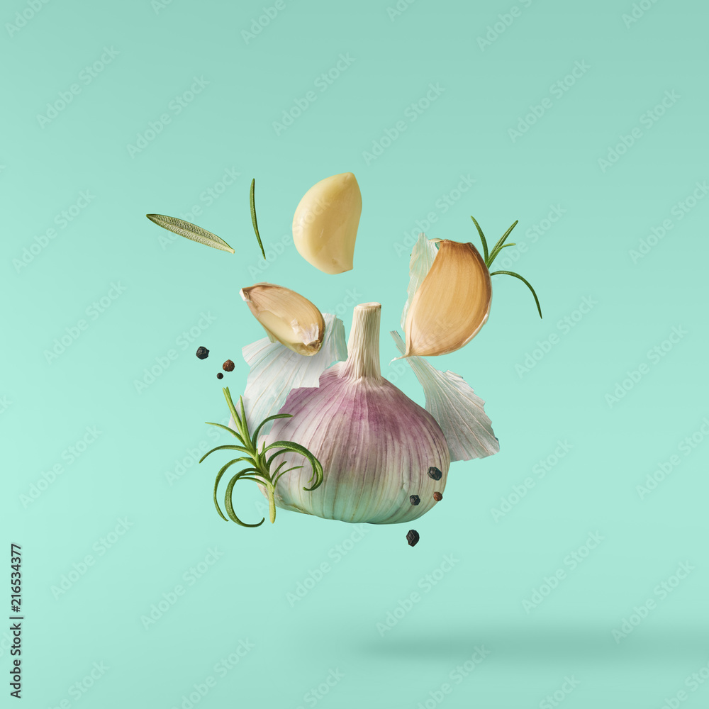 Garlic falling in air with pepper and herbs like rosemary on turquoise ...