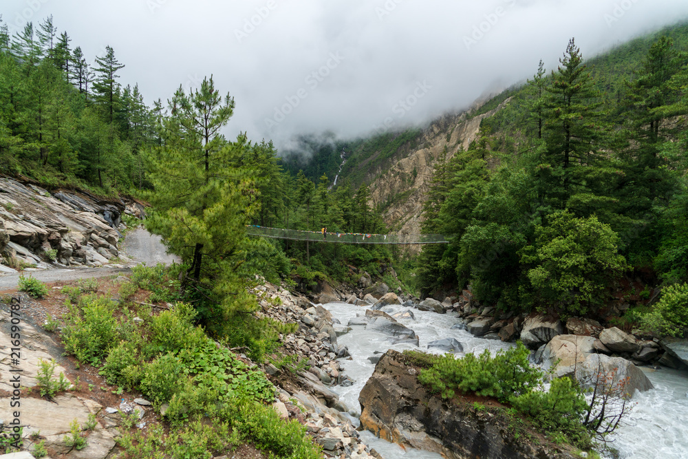 A swinging suspension bridge crosses the Marsyangdi River in Nepal on ...