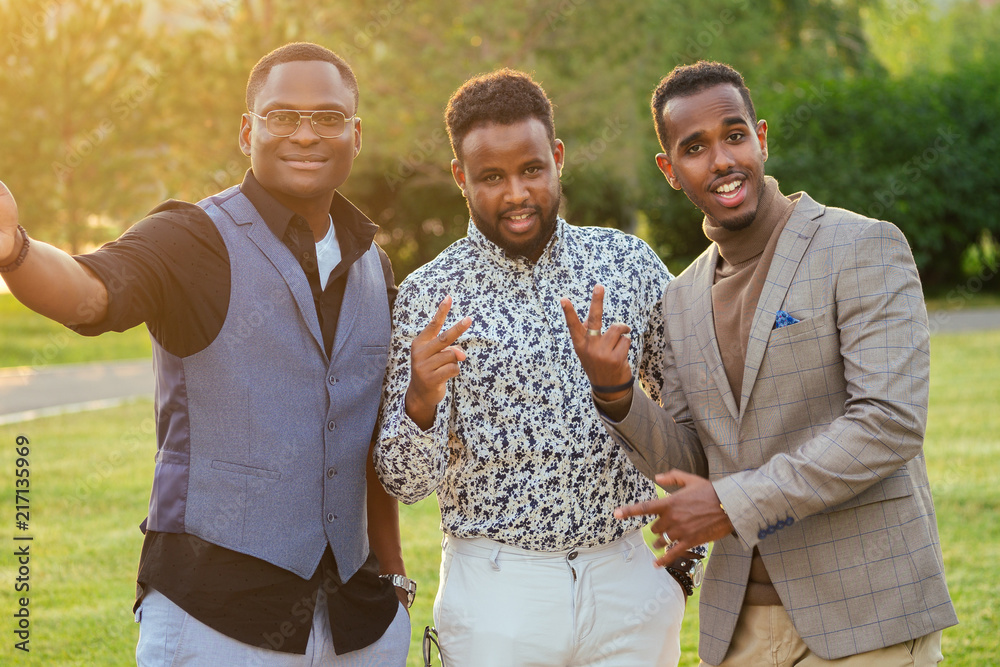 a group of three black men in stylish suits in a summer park. African ...
