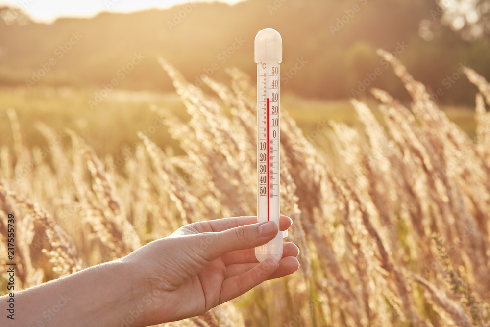 Global warming concept. Womans hand holds thermomemter which measure very high temperature ...