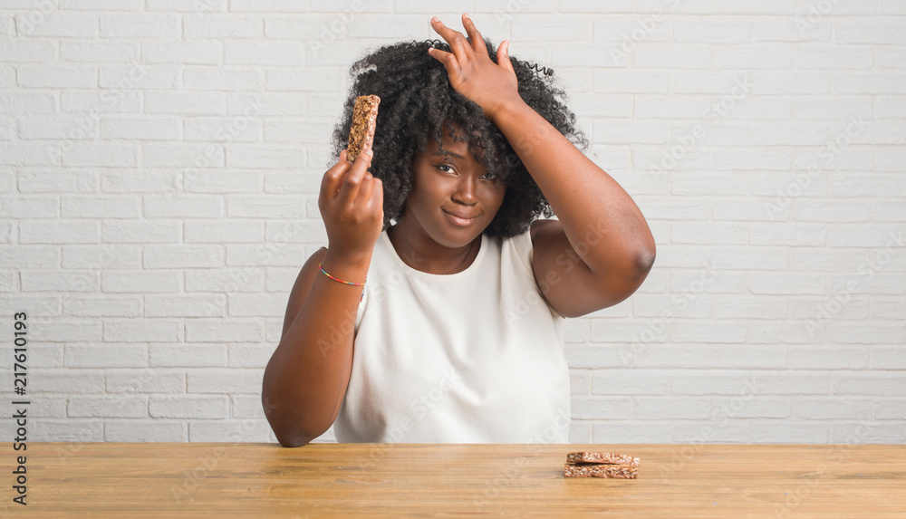 Young african american woman sitting on the table eating cereal bar ...