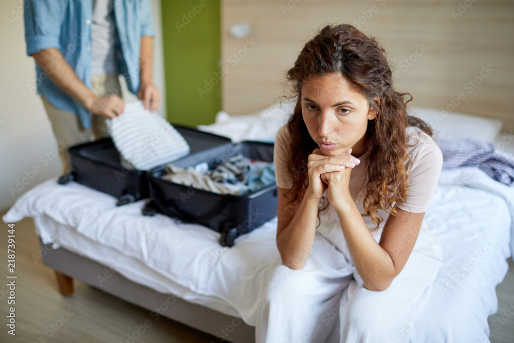Stressed young woman sitting on bed while her husband preparing ...