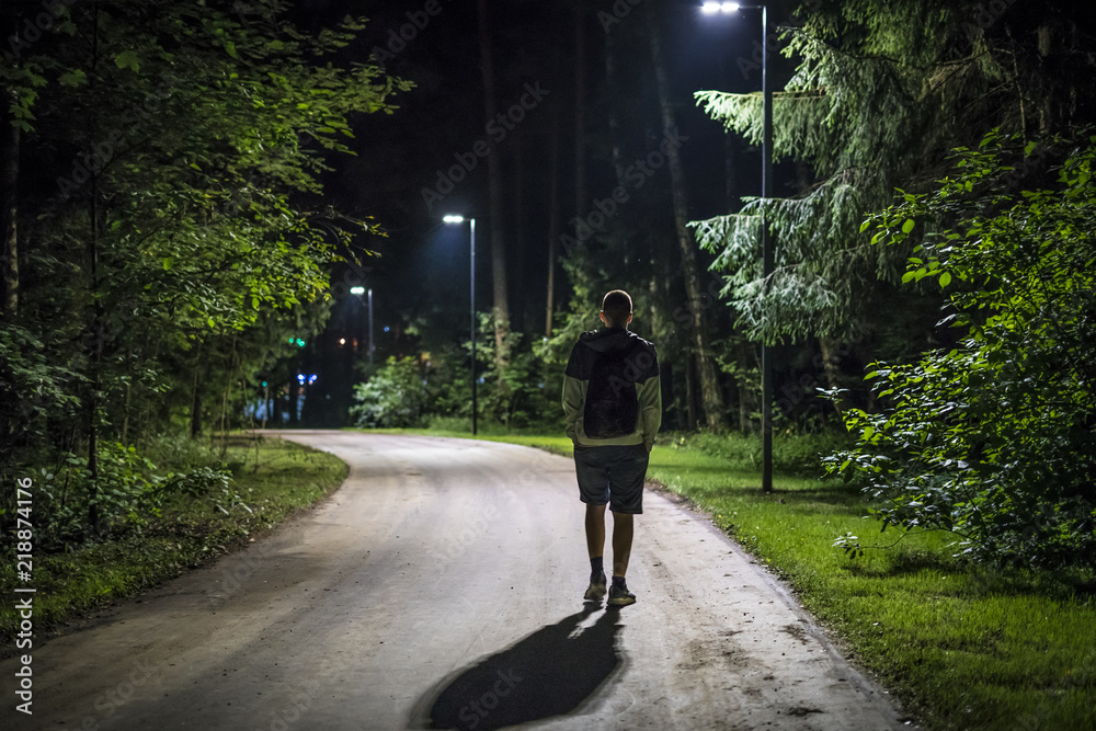 alone young man in casual walking on the night forest road with the ...