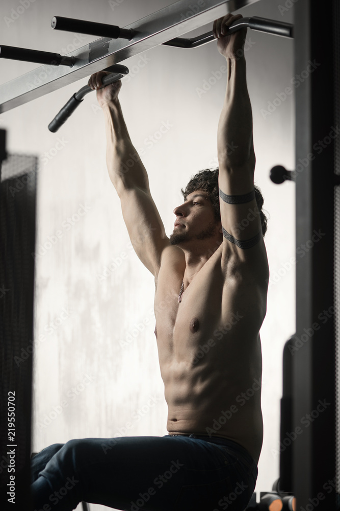 bodybuilder on the bar raises his legs up, exercises on the press in ...