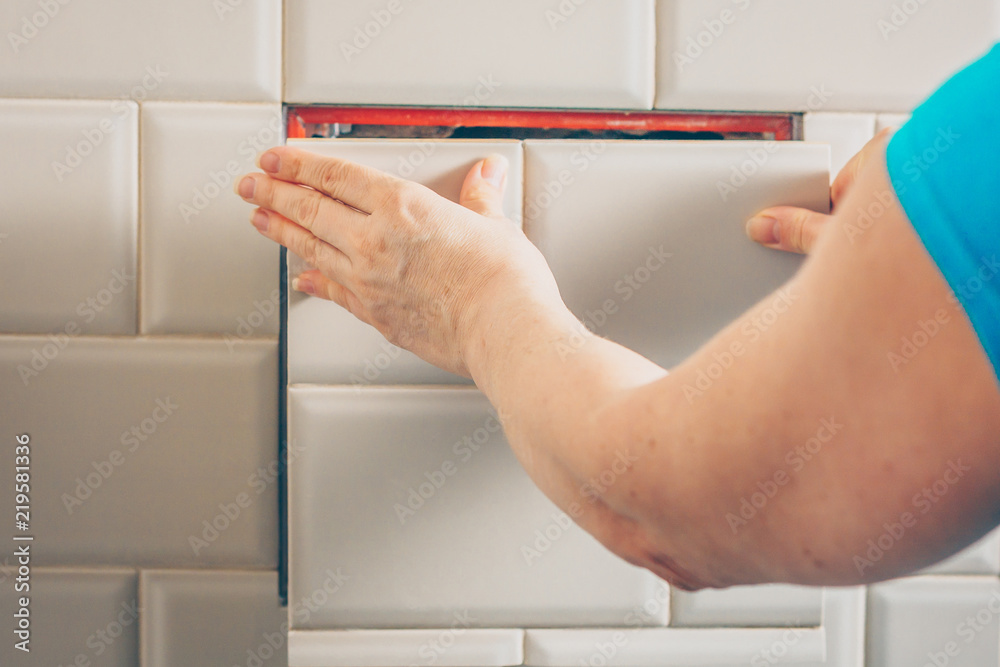 Stock-Foto „The girl opens a hidden hatch on the wall of the tile to ...