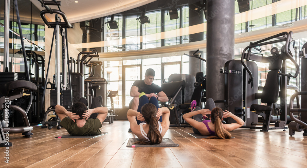 Fitness instructor timing three young people doing lateral crunch ...
