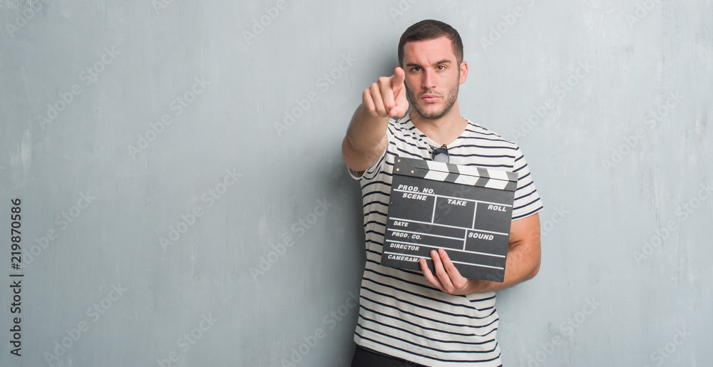 Young caucasian man over grey grunge wall holding movie clapboard ...