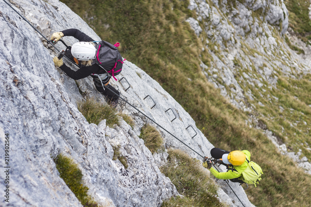 Woman and group of other people climbing on steep rock face on via ...