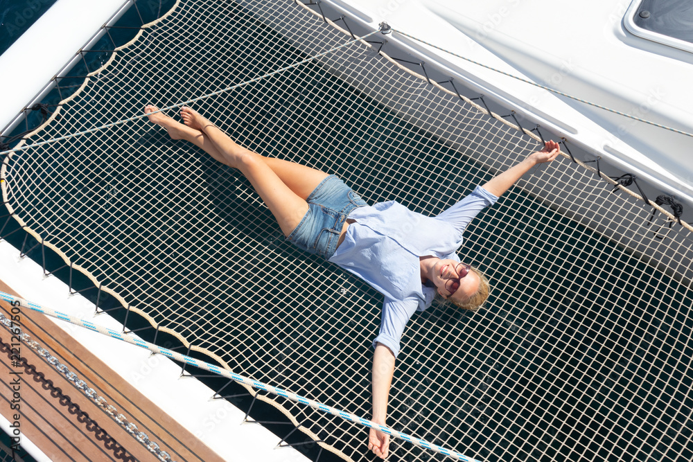 Casualy dressed woman relaxing, lying in hammock of a catamaran sailing ...