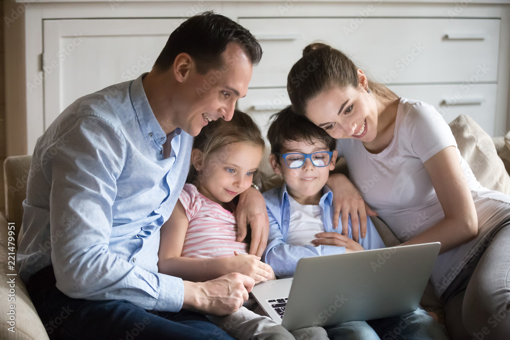 Happy family of four sit together on couch watching cartoons on laptop ...