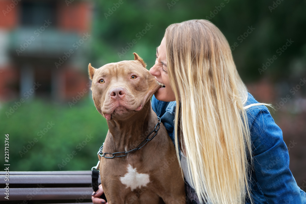 Fotografie Funny owner girl biting a pit bull terrier dog on the cheek ...
