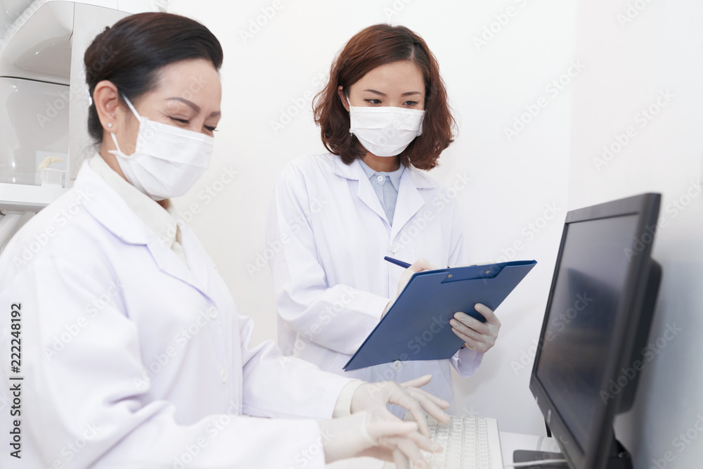 Dentist reading medical record aloud and nurse entering information in ...