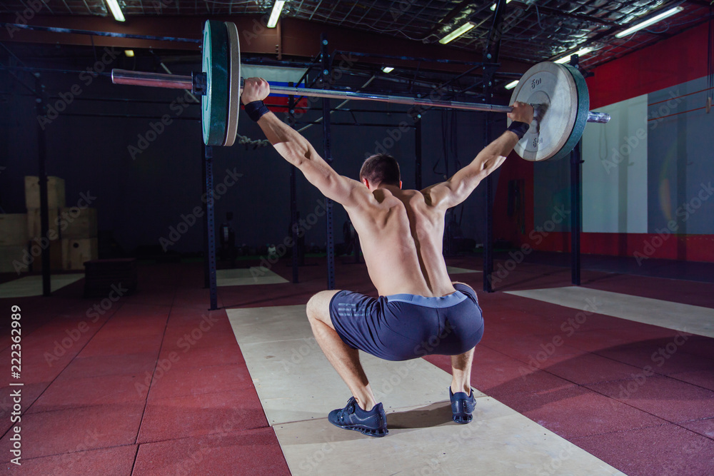 sporty man performing overhead squats with a heavy barbell at the gym ...