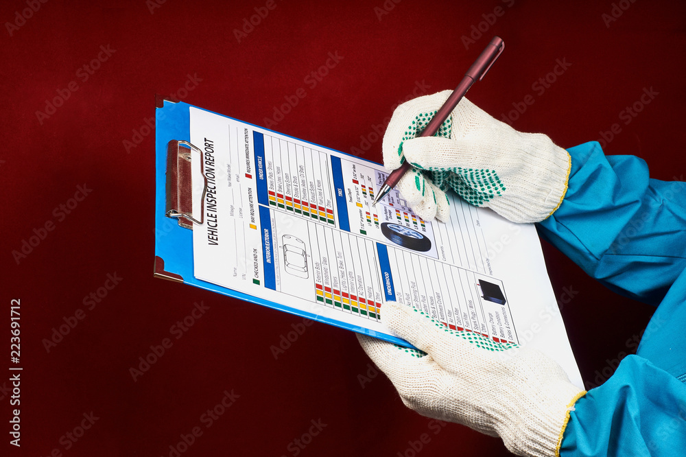 mechanic writes in the vehicle inspection report form on a red velvet ...