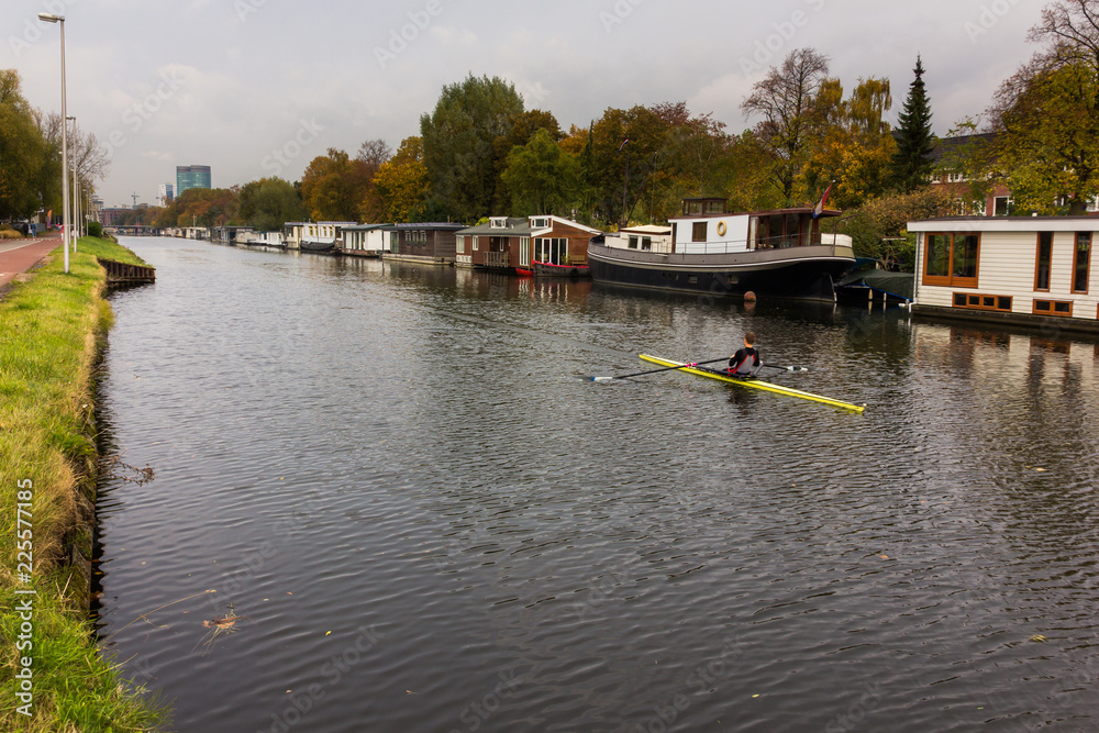 Single scull rowing on a channel full of houseboats (Utrecht ...