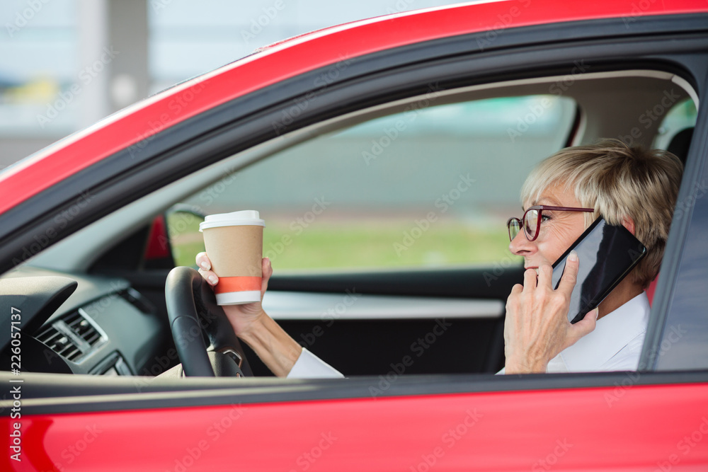 Reckless, smiling mature woman talking on the phone and holding a cup ...