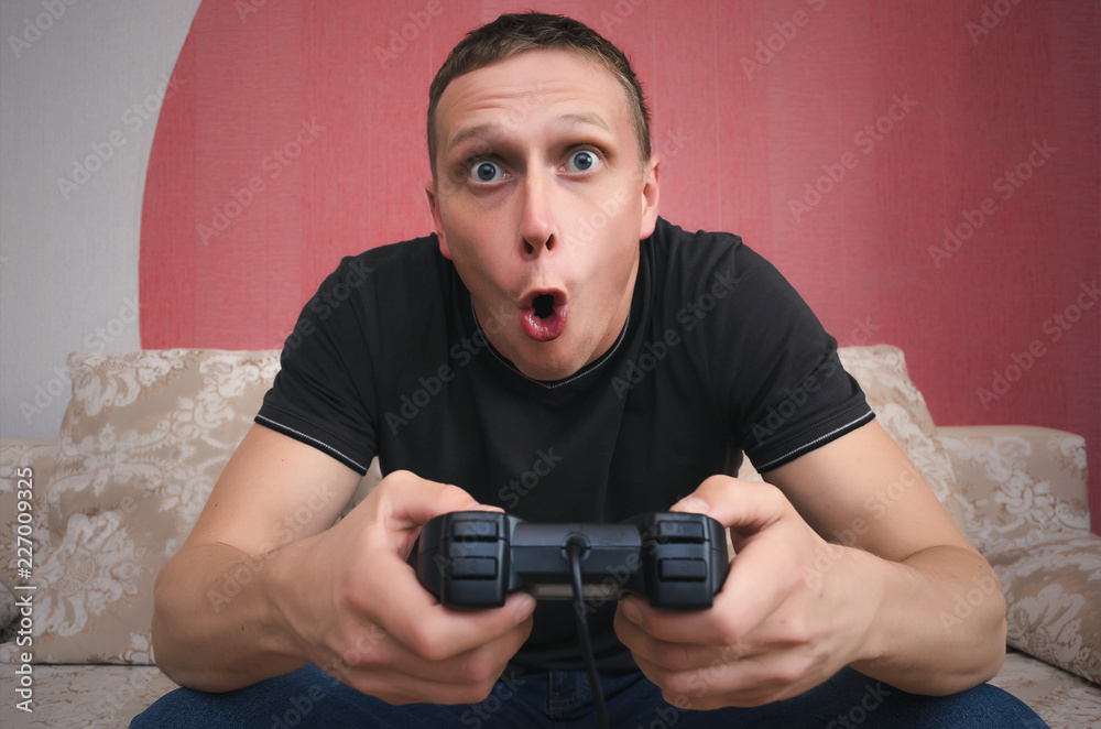 Surprised and enthusiastic gamer man with a joystick in his hands is ...