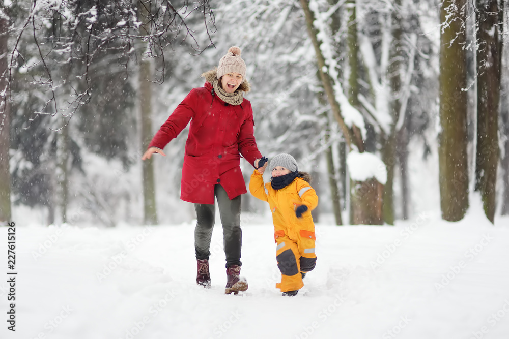 Beautiful mother and his son walking in winter park during snowfall ...