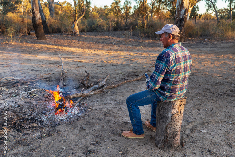 Mature man sitting on stump and enjoying a beer as he contemplates the ...