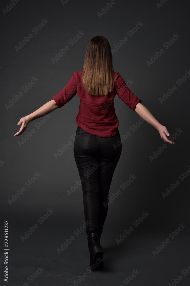 full length portrait of brunette girl wearing red shirt and leather pants. standing pose, facing ...