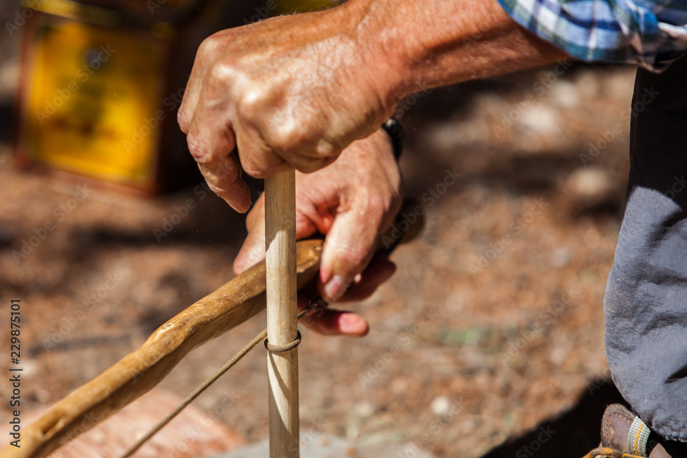 Native man is lighting a campfire using the hand drill technique and ...