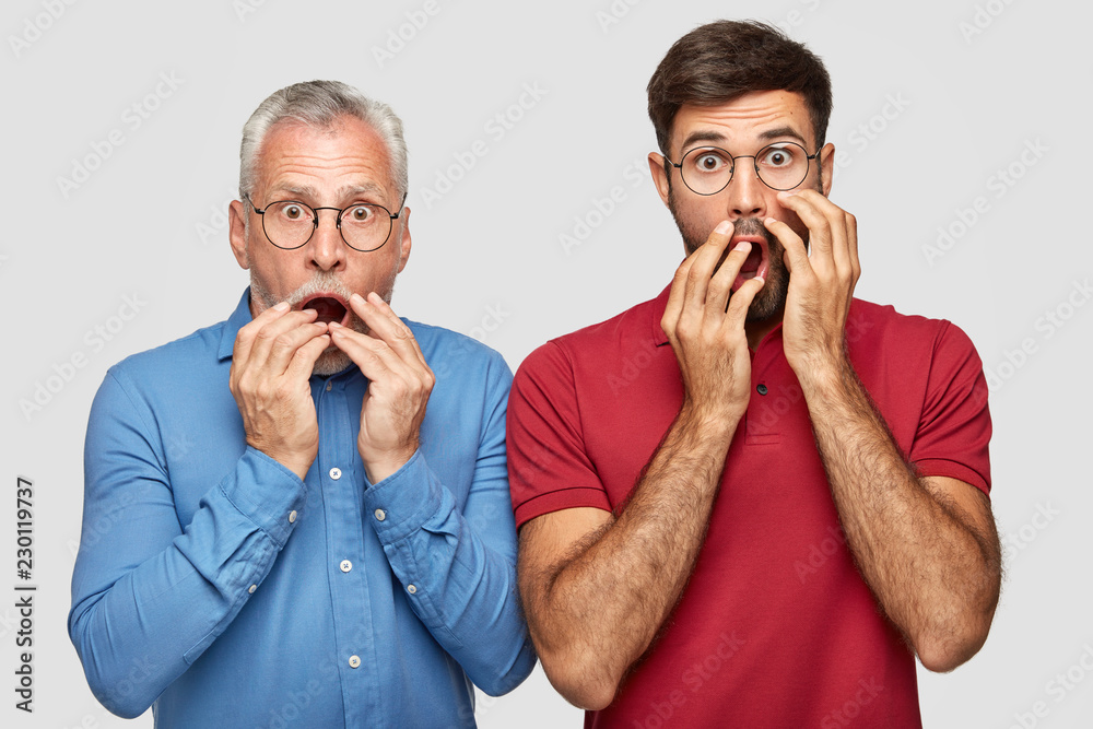 Shocked emotive father and son look with scared expressions, keep hands ...
