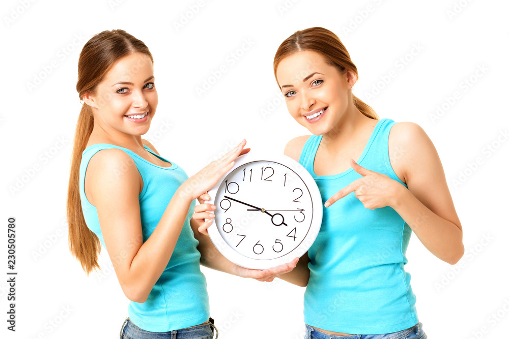 Two smiling women holding a clock. Twins, girls models are surprised ...
