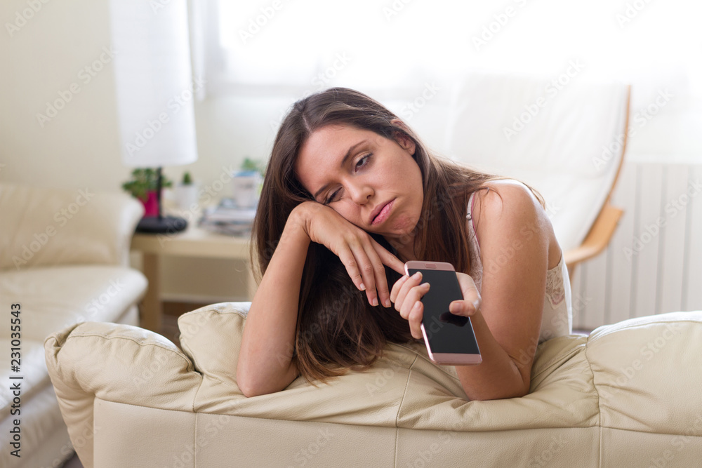 European brunette woman showing fatigue holding her cell phone with ...