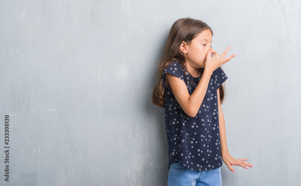Young hispanic kid over grunge grey wall smelling something stinky and ...