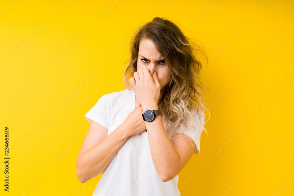 Young beautiful blonde woman over yellow background smelling something ...