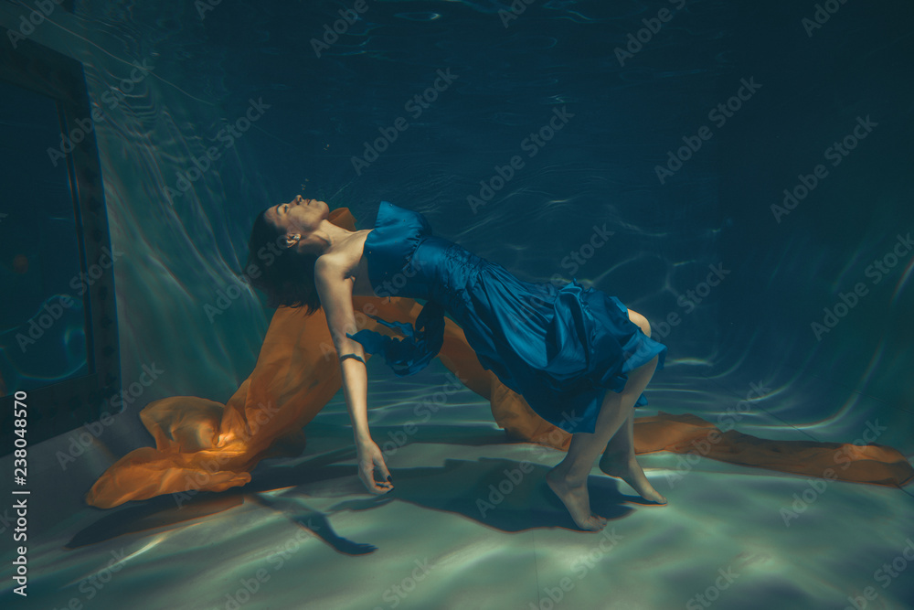 cute sporty female swims underwater as a free diver in a blue evening ...
