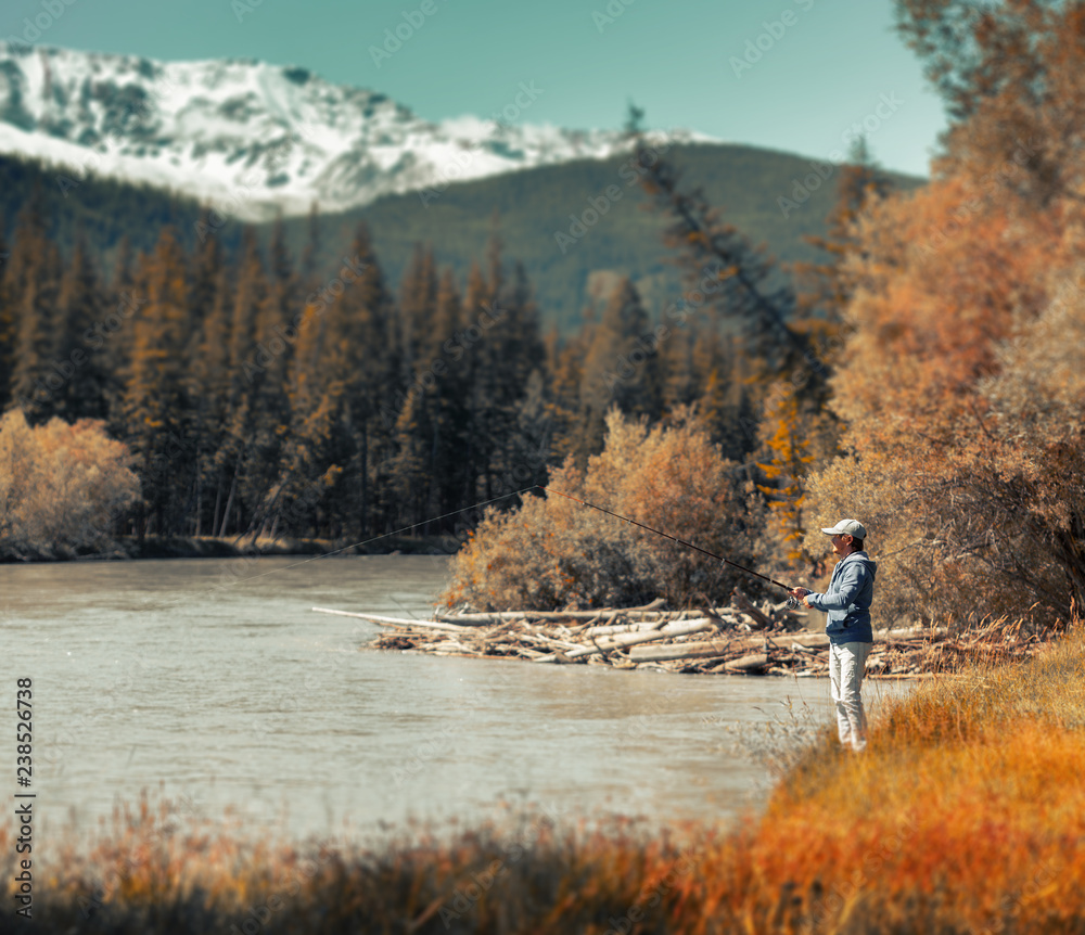 Young amateur angler fishing in the rapid river with snow caped ...