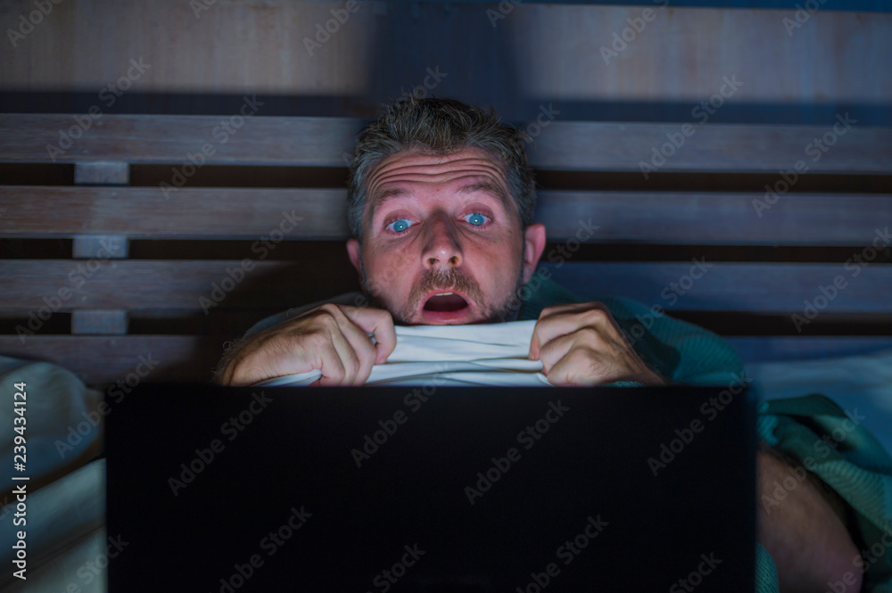 young scared and stressed man in bed watching internet horror movie ...