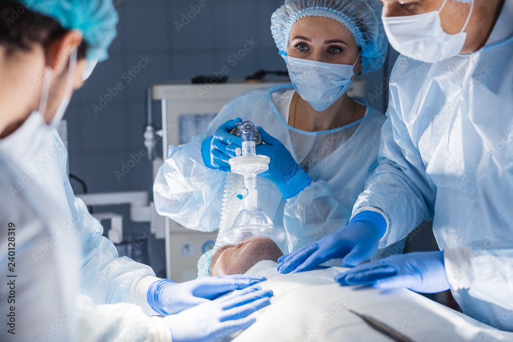 Female nurses putting oxygen mask on patient in operation room. Pre ...