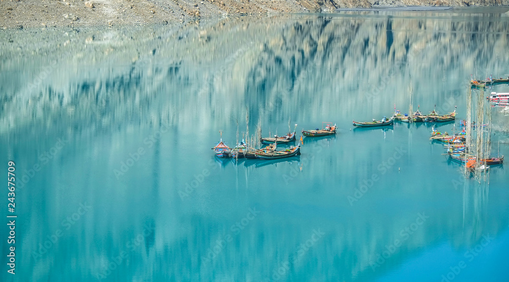 Docked boats in the turquoise Attabad lake with reflection of mountain ...