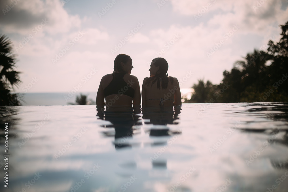 Two young lesbian girls at sunrise in an outdoor pool in the tropics ...