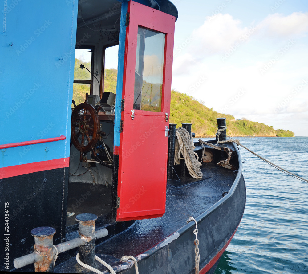A brightly painted red, blue, and black tug boat tied to a dock, with ...