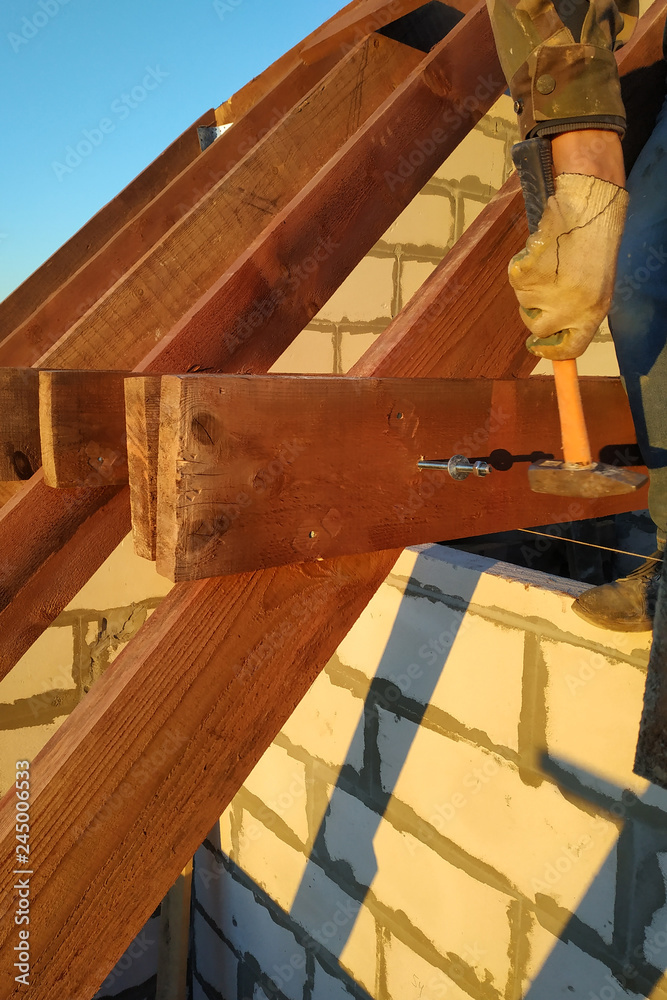 The worker claps the studs with a hammer on the rafters, building a ...