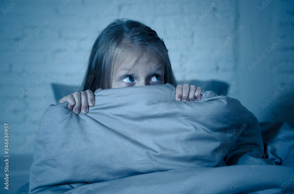 Sleepless cute girl in fear at night hiding behind the blanket afraid ...