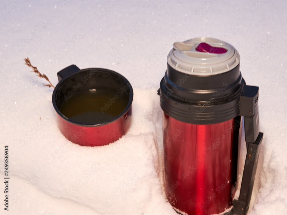 big red tea thermos with the lid open on the snow in the woods in the ...