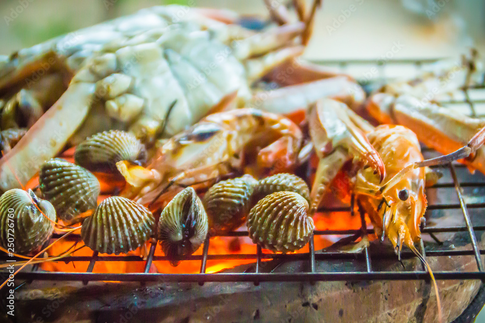 Close up grilled crabs and clams on fire charcoal stove at night party ...