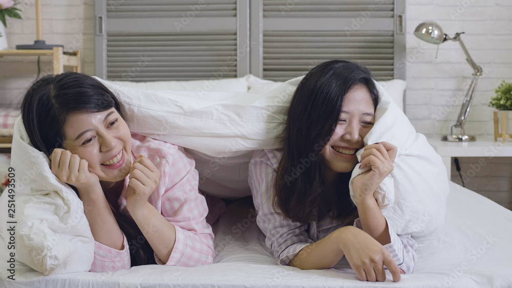 group of asian women roommates lying in bed under quilt smiling lovely ...