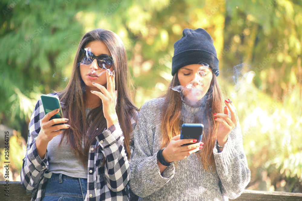 two girls smoking cigarettes and using smart phones. concept of ...
