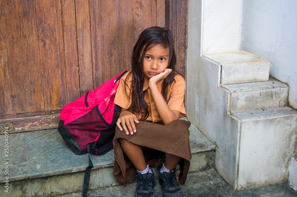 7 or 8 years child in school uniform sitting outdoors sad and depressed ...