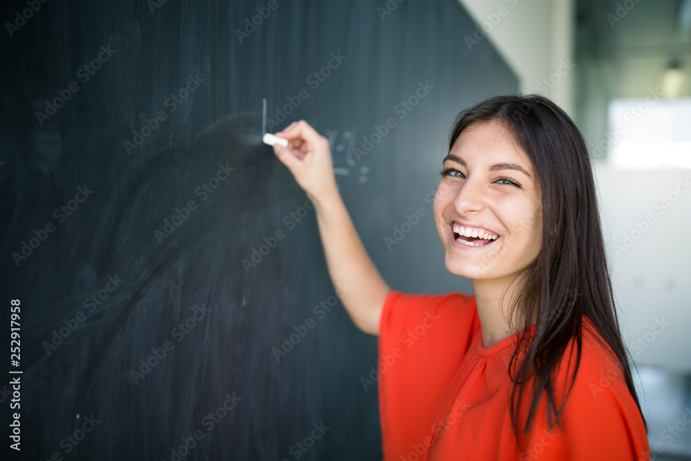 Pretty, young college student writing on the chalkboard/blackboard ...