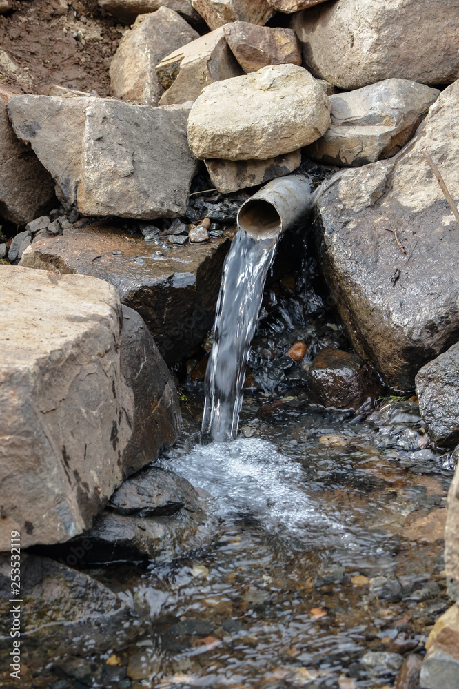 Spring water pours from a pipe that is buried deep underground. Water ...